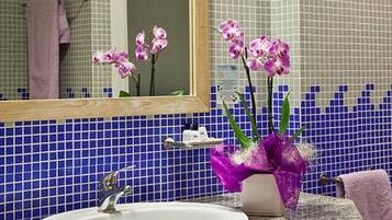 Casa de banho com lavatório, espelho e orquídeas roxas.
