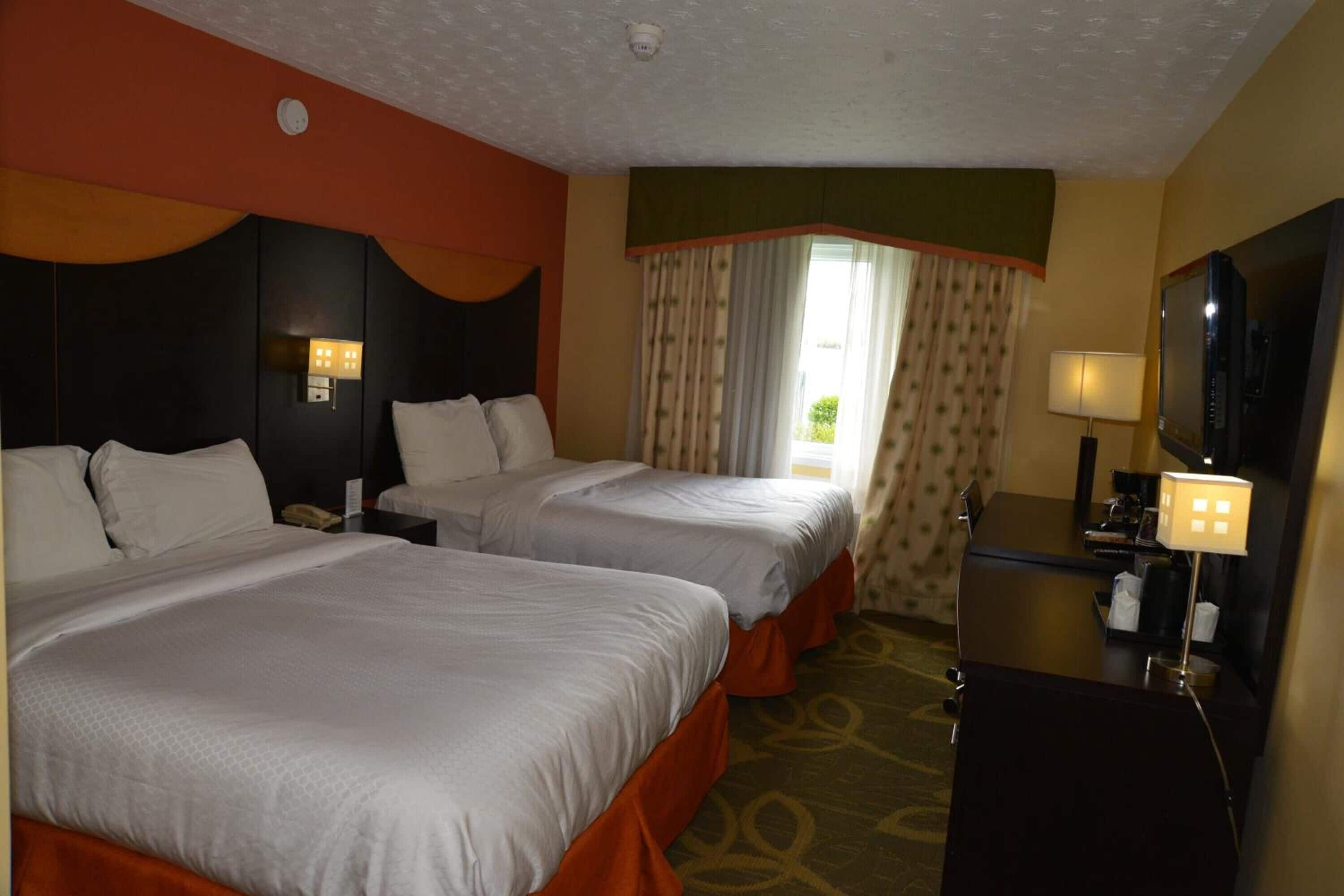 Quarto de hotel com duas camas, uma escrivaninha, televisão e janela com cortinas.
