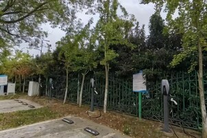 Uma área de estacionamento com postos de carregamento para veículos elétricos, cercas e uma placa.