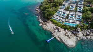 Vista aérea de um hotel à beira-mar, com vários edifícios, piscina e um trecho de costa rochosa.