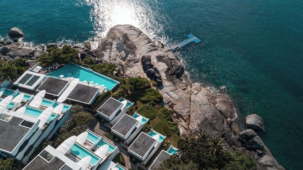 Vista aérea de um resort com várias piscinas, uma costa rochosa e um píer que se estende para o mar.