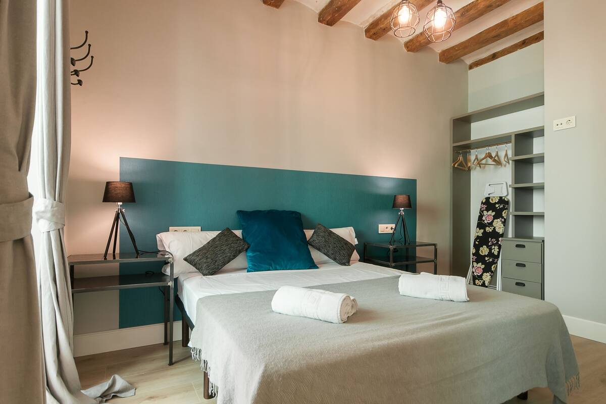 Quarto bem arrumado com cama, mesas de cabeceira, guarda-roupa e luminária pendente.
