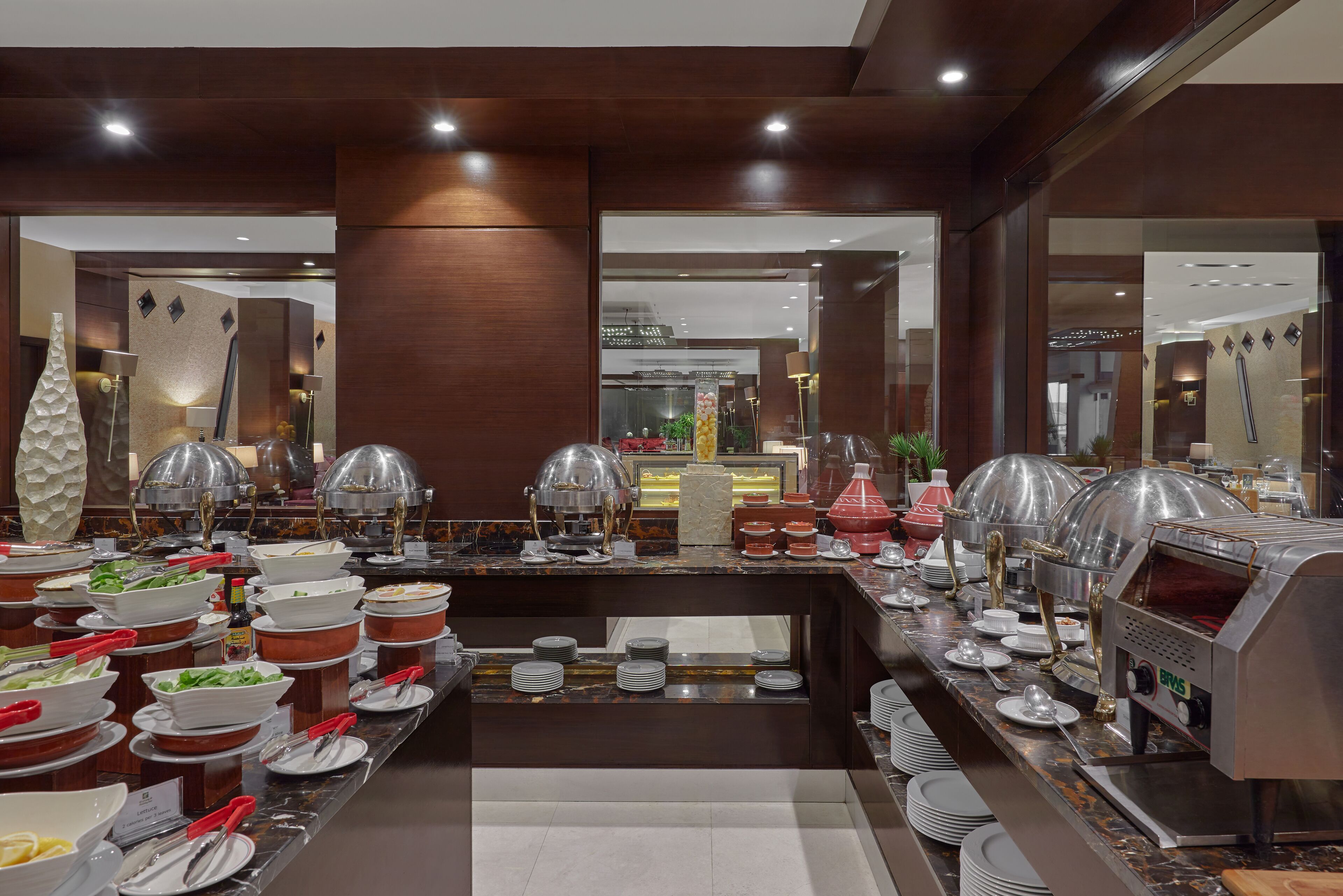 Disposição de buffet com diferentes estações de comida, incluindo saladas, frutas e pratos quentes, dispostos sobre um balcão de mármore.