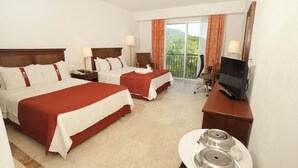 Quarto de hotel com duas camas, televisão, mesa de jantar com bandeja e varanda com vista.