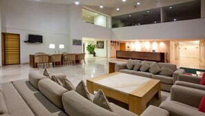 Uma área de estar ampla com teto alto, um balcão de recepção e um espaço de estar com sofás e uma mesa de centro.
