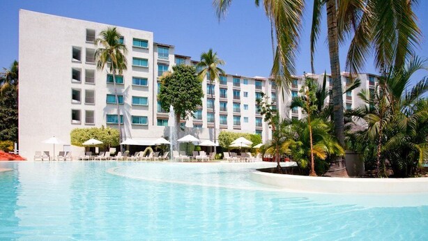 Um hotel com piscina, palmeiras e espreguiçadeiras.