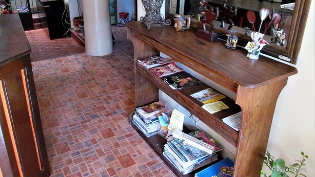Um console de madeira com revistas, uma luminária e um espelho.