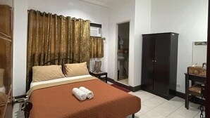 Quarto de hotel com uma cama, guarda-roupa, mesa pequena e espelho.