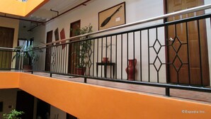 Interior com vários níveis, corrimão de varanda, portas de madeira e plantas em vasos.