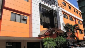 Um edifício moderno com paredes externas em laranja e branco, grandes janelas e uma área de entrada coberta com palmeiras.