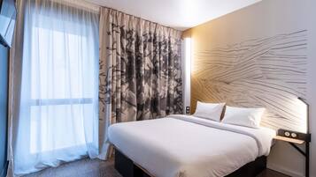 Quarto de hotel com cama grande, cortinas leves, cortina estampada, design de arte na parede e mesa de cabeceira com luminária.