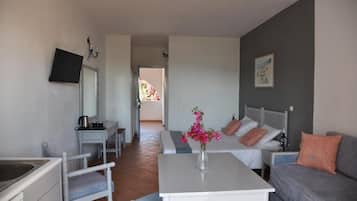 Quarto de hotel pequeno com cama, sofá, mesa pequena, escrivaninha e televisão fixada na parede.