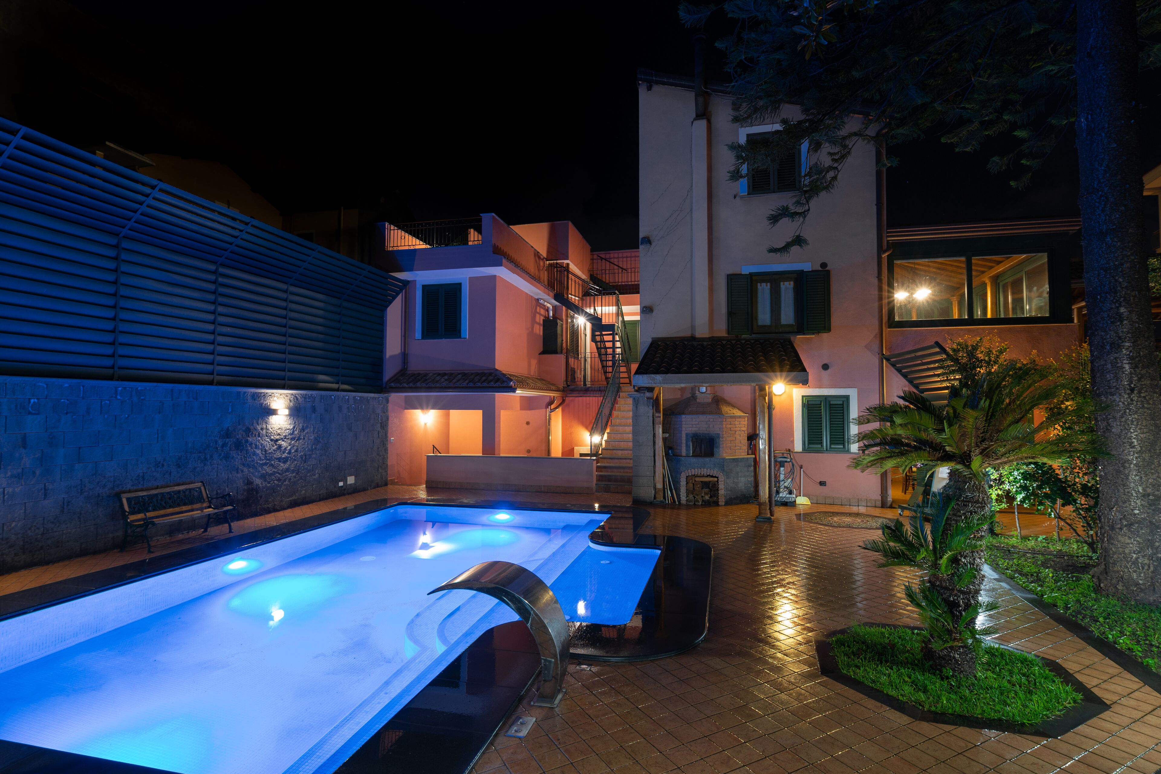 Piscina ao ar livre com um banco, cercada por edifícios com varandas e uma escadaria que leva aos andares superiores.