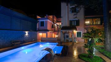 Piscina ao ar livre com um banco, cercada por edifícios com varandas e uma escadaria que leva aos andares superiores.