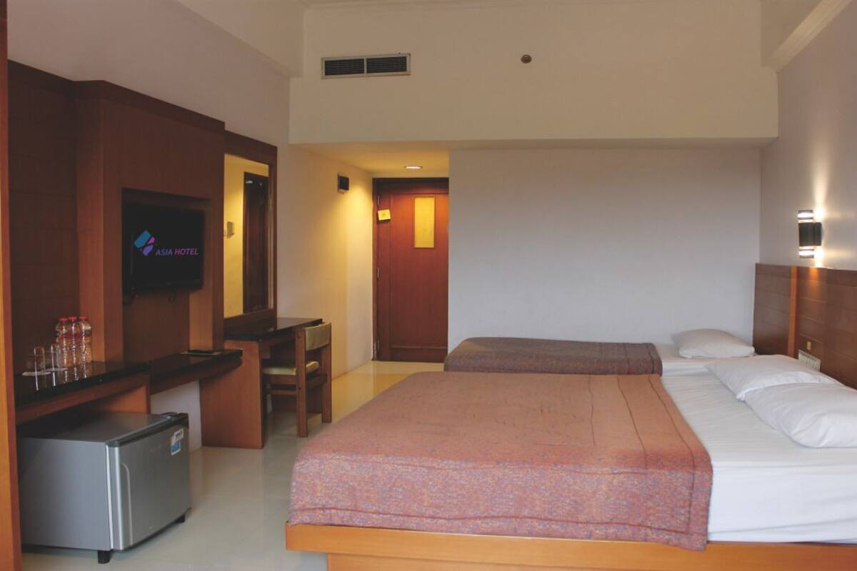 Quarto de hotel com cama, escrivaninha com computador, televisão e minibar.