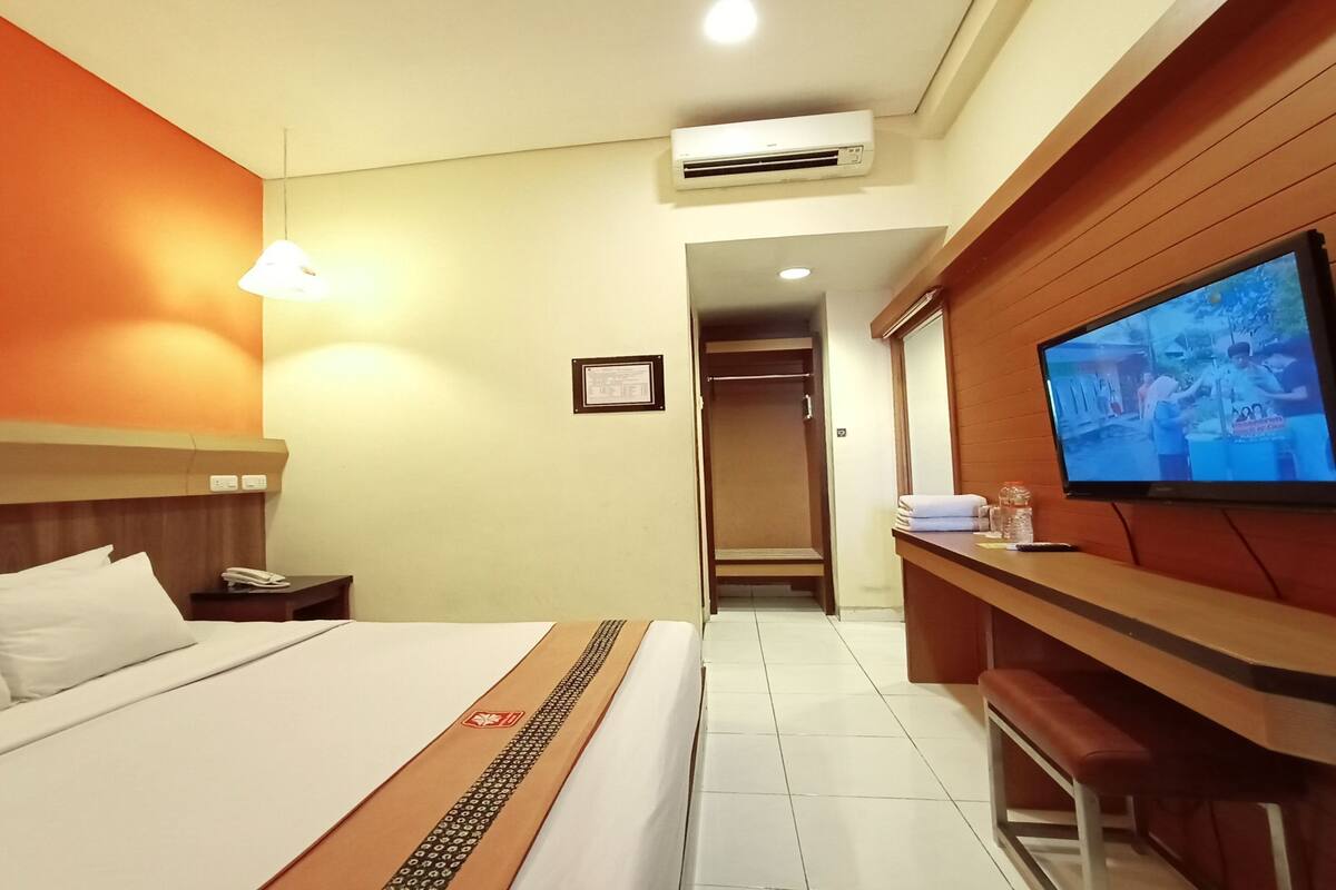 Quarto de hotel com cama, televisão, escrivaninha e ar condicionado.