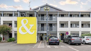 Um hotel com um letreiro amarelo chamativo, vários andares e um estacionamento com carros.