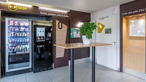 Uma área de recepção de hotel com uma máquina de venda automática, uma mesa com planta em vaso e uma porta com um mapa.