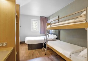 Quarto compacto com duas beliches, porta de madeira, janela com cortinas e uma pequena mesa de cabeceira.