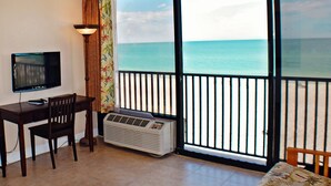 Quarto com televisão, secretária, cadeira, ar condicionado e vista para o oceano através de grandes portas deslizantes.
