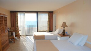 Quarto de hotel com duas camas, uma mesa e vista para o mar.