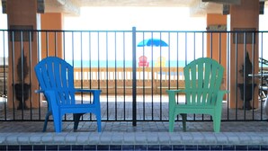 Duas cadeiras junto a uma piscina, um corrimão e vista para o mar.
