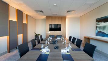 Sala de conferências com uma mesa comprida, cadeiras, placas de identificação e uma tela de televisão.