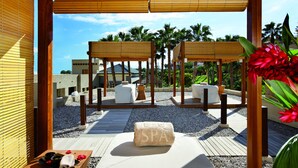 Uma área de spa com pérgulas de madeira, uma toalha branca com a inscrição 'SPA' e uma bandeja com uma tigela e uma garrafa.