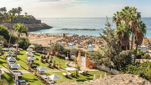 Um resort com área de praia, palmeiras e vista para o mar.