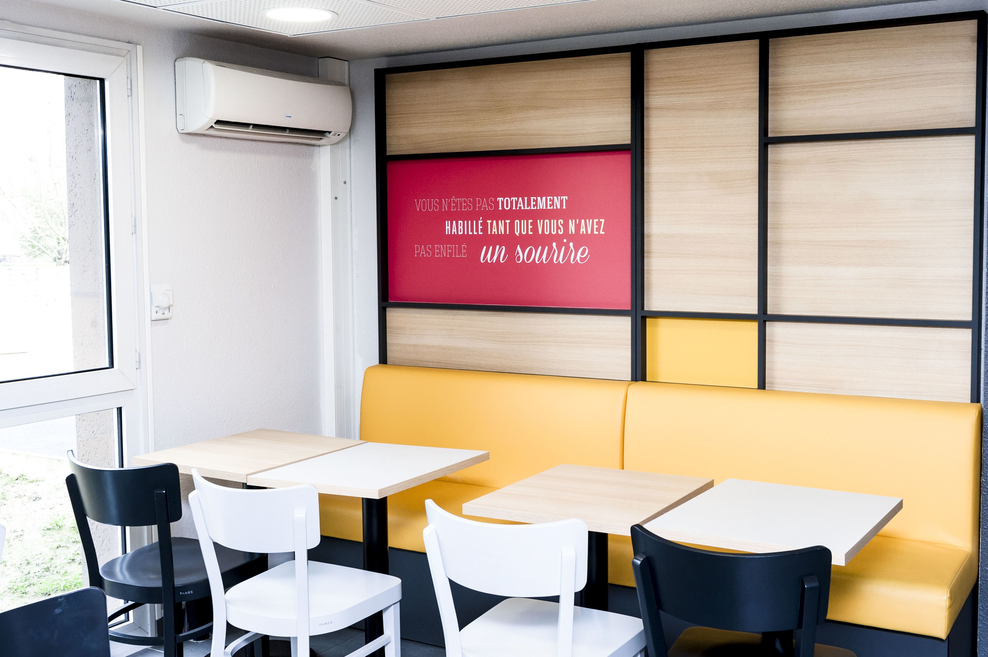 Interior de restaurante com assentos em amarelo, mesas brancas e cadeiras pretas.