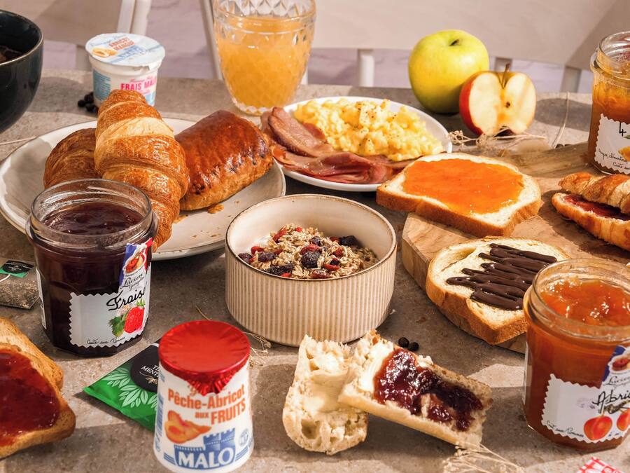 Uma mesa de café da manhã com croissants, presunto, ovos e diversas geleias.