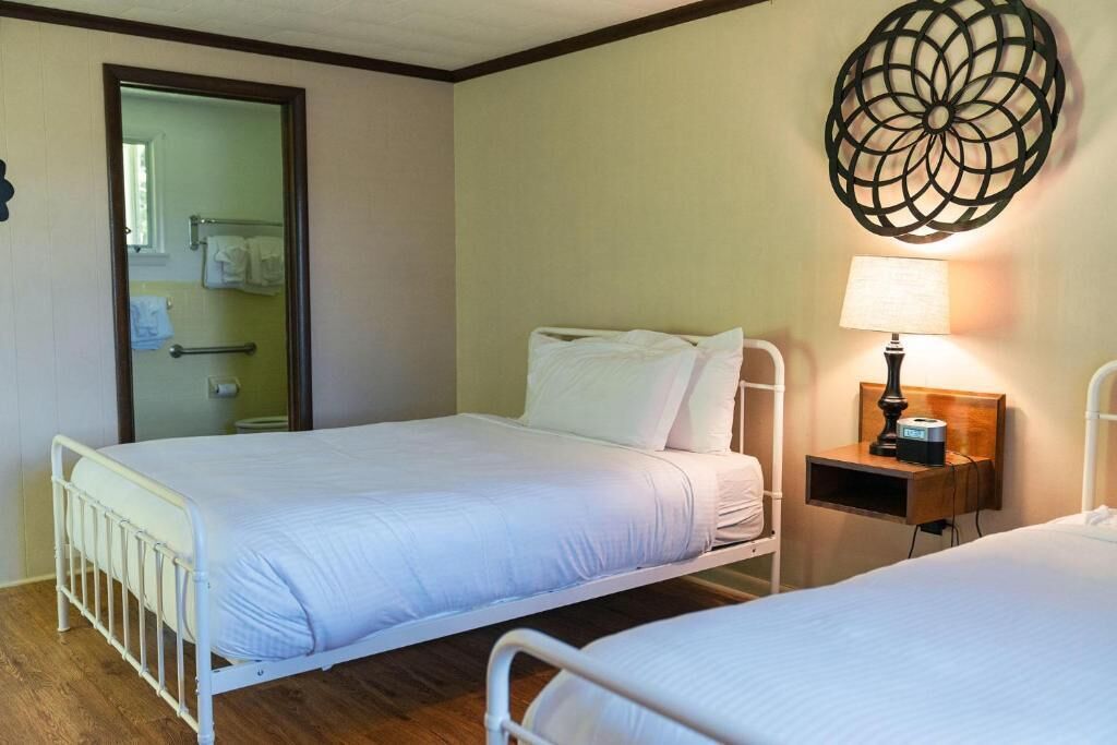 Quarto com duas camas de solteiro, mesa de cabeceira com abajur e um objeto decorativo na parede.