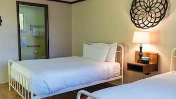Quarto com duas camas de solteiro, mesa de cabeceira com abajur e um objeto decorativo na parede.