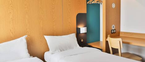 Quarto de hotel com duas camas, uma escrivaninha, uma cadeira e um guarda-roupa com roupas penduradas.