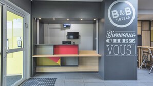 Uma receção com um ecrã digital, uma televisão de ecrã plano e um letreiro com a inscrição "B&B Hotels" e "Bienvenue Chez Vous".