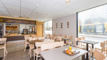 Um café com mesas e cadeiras, um balcão com menu e uma janela com vista para a rua.