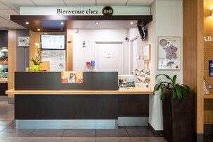 Balcão de recepção com tela digital, quadro de menu e uma planta.