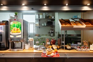 Buffet de café da manhã com máquina de café Granini, diversos alimentos e micro-ondas.