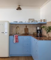 Uma cozinha com armário azul, geladeira branca, cafeteira e toalha pendurada.