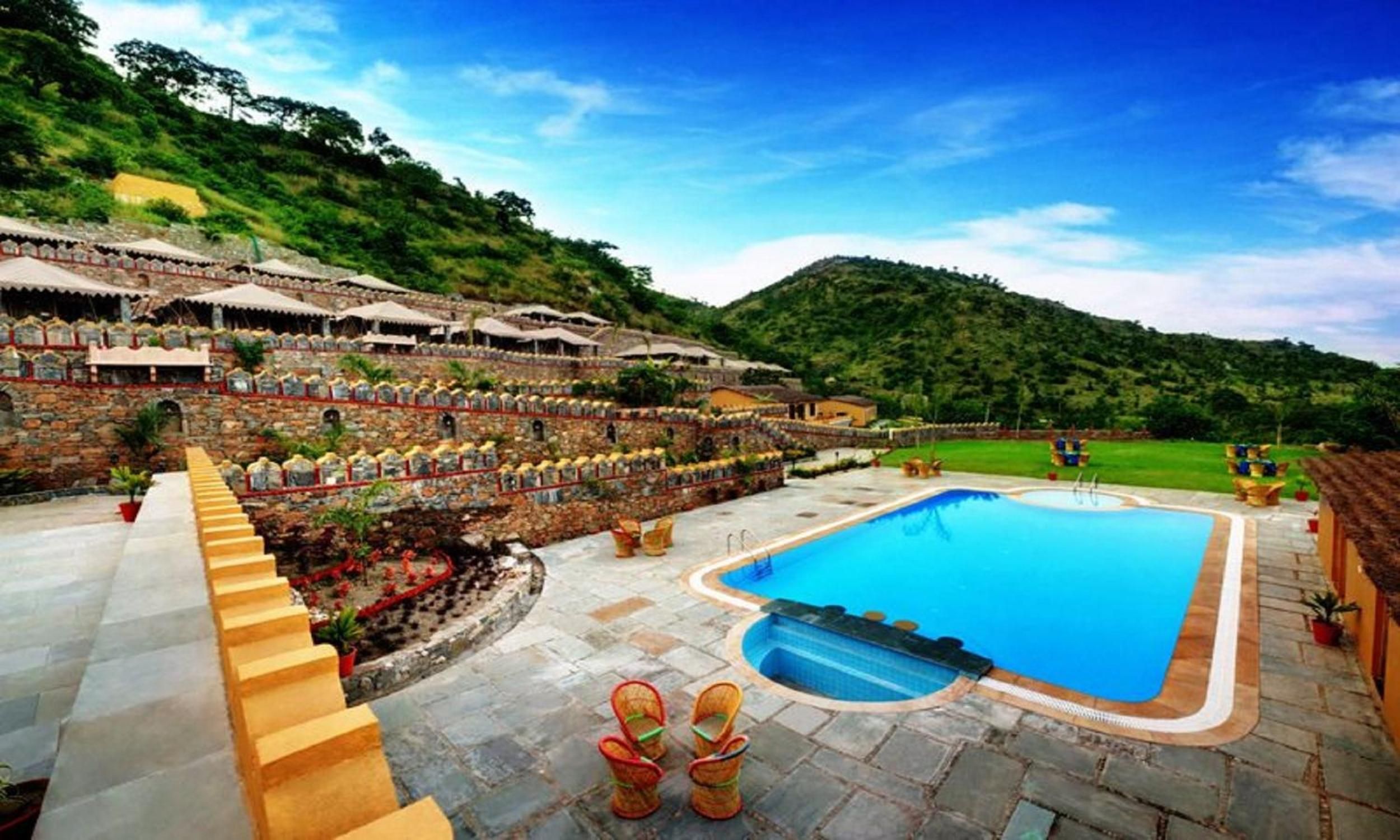 Área de piscina com deck de pedra, piscina e encosta ao fundo.