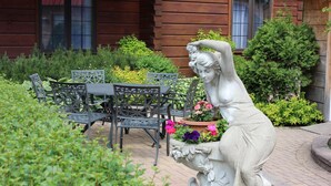 Um jardim com uma estátua, área de estar externa e um edifício ao fundo.