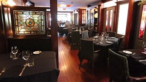 Interior de restaurante com mesas postas para refeições, uma janela de vitrais e piso de madeira.