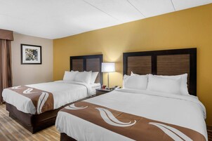Quarto de hotel com duas camas, uma mesa de cabeceira com abajur e um quadro na parede.
