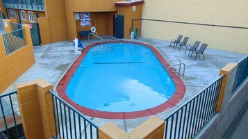 Piscina externa com borda vermelha, rodeada por um deck de concreto e corrimãos de metal.