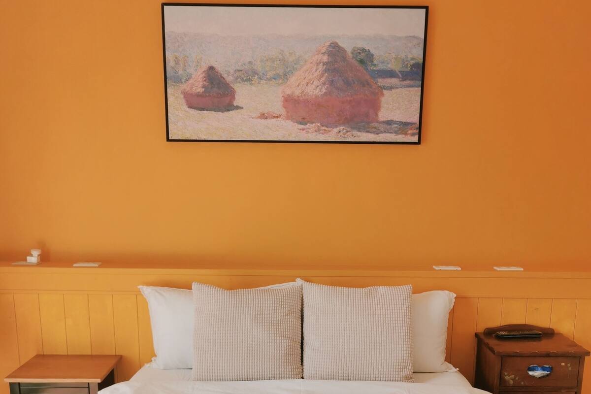Cama bem arrumada com roupa de cama branca, cabeceira de madeira e mesa de cabeceira com controle remoto.