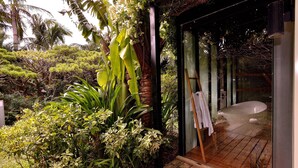 Um deck de madeira que leva a uma porta de vidro, onde se pode ver uma banheira no interior.