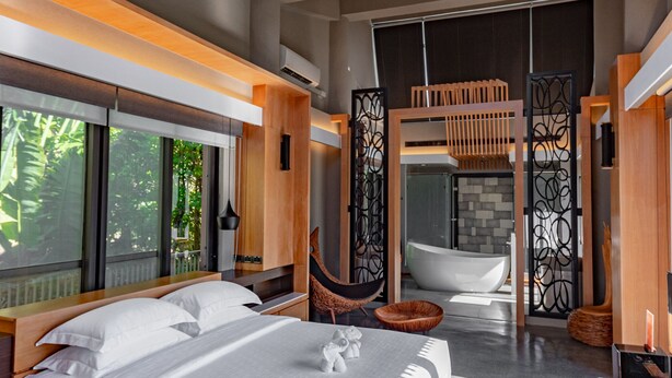Quarto moderno com uma cama grande, um banco de madeira, uma banheira e vista para o verde.