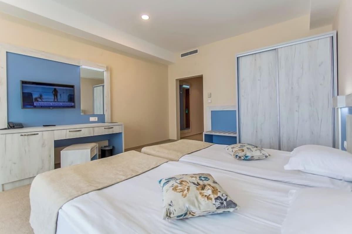 Quarto de hotel com duas camas, uma escrivaninha, televisão e um guarda-roupa.