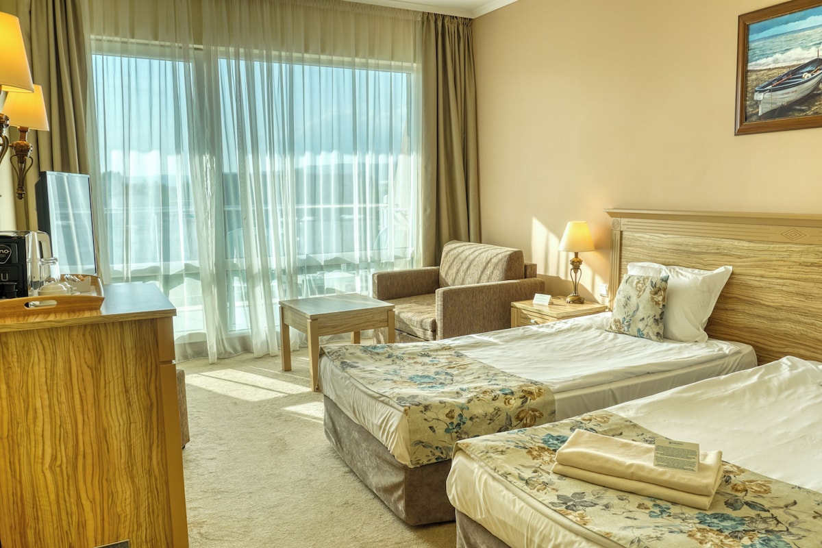 Quarto de hotel com duas camas, uma escrivaninha, uma cadeira, uma máquina de café e um quadro na parede.