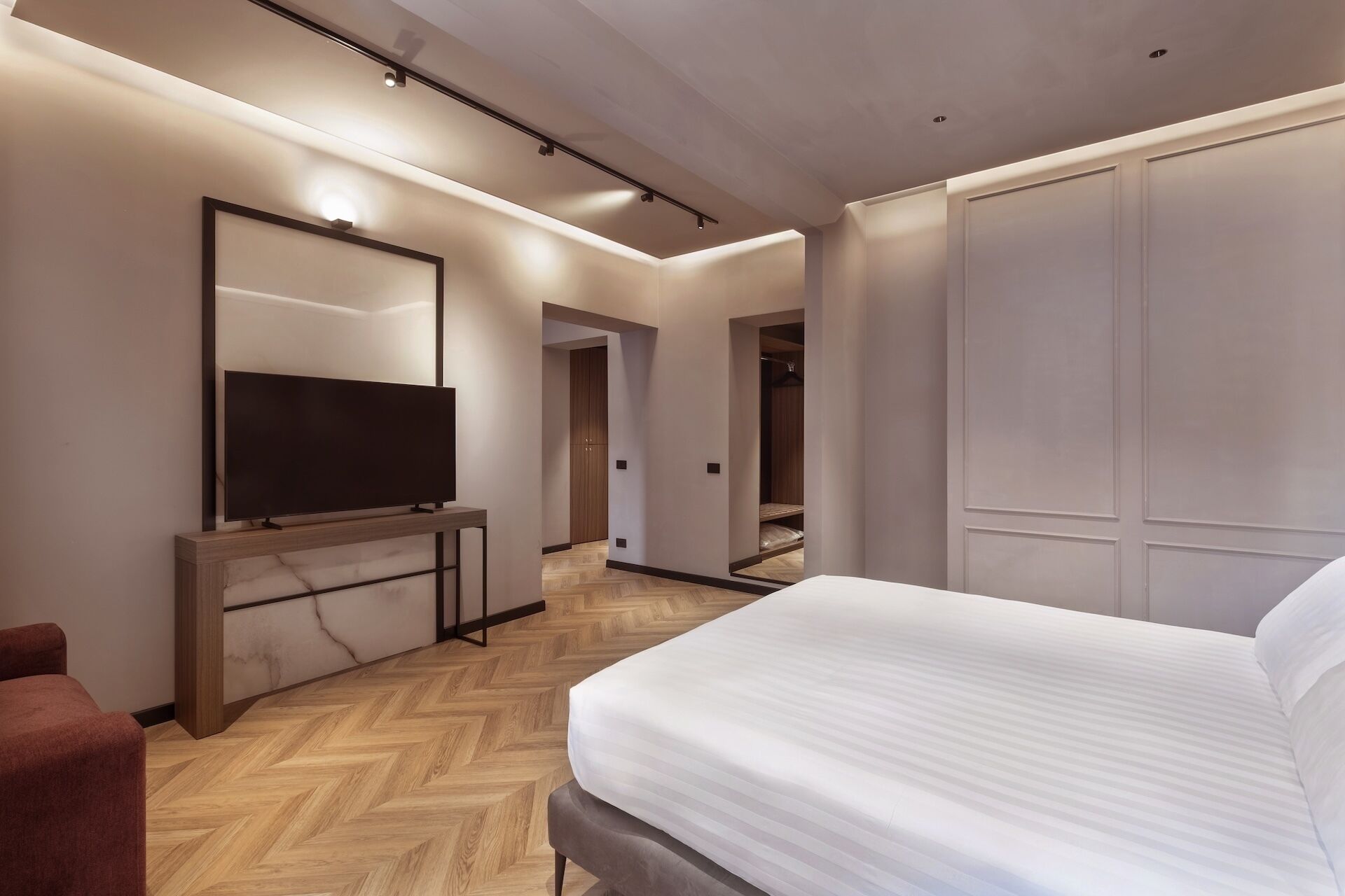 Quarto de hotel moderno com uma cama grande, uma televisão de tela plana sobre um console de madeira, um guarda-roupa e um piso com padrão losango.